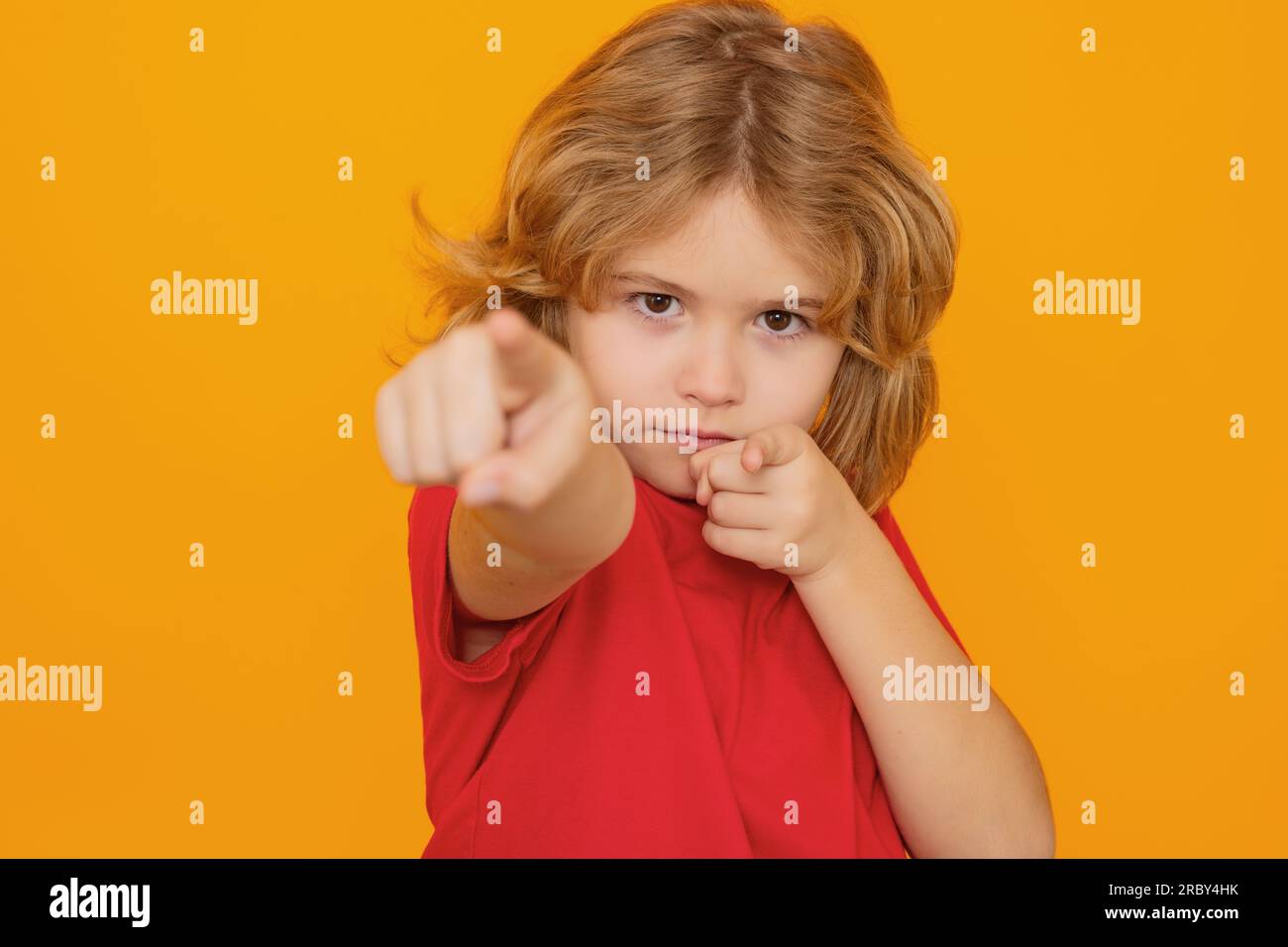 Portrait of child in red t-shirt pointing you on yellow isolated studio ...