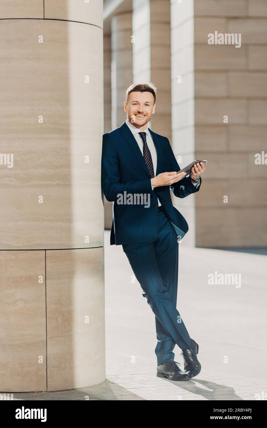 Photo of cheerful male dressed in expensive black suit, stands crossed ...