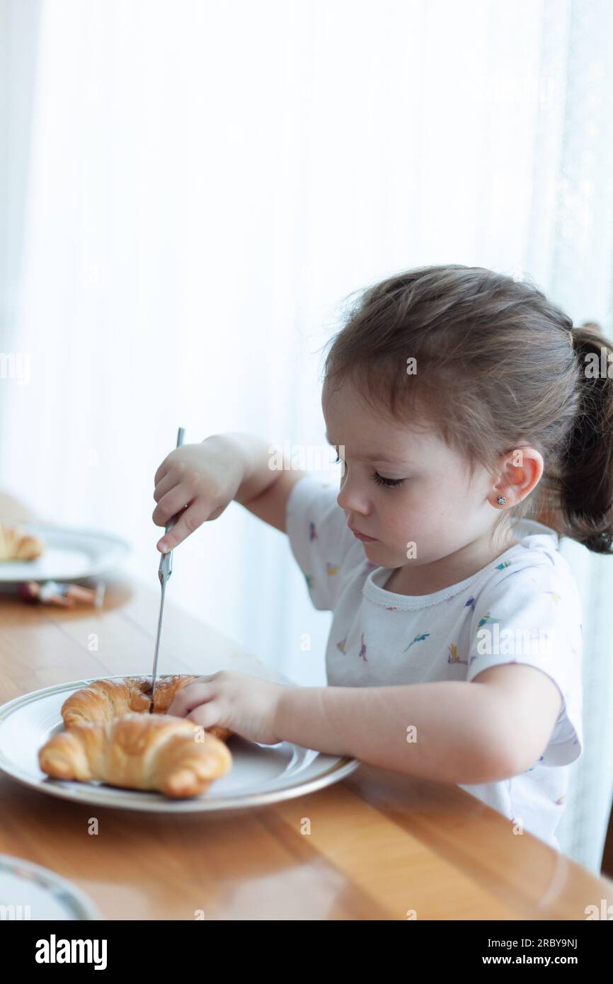Cute little girl eating croissant in the morning at home Stock Photo ...
