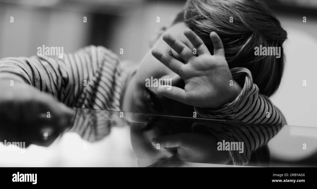 Sad depressed child leaning on table covering face with hand in ...
