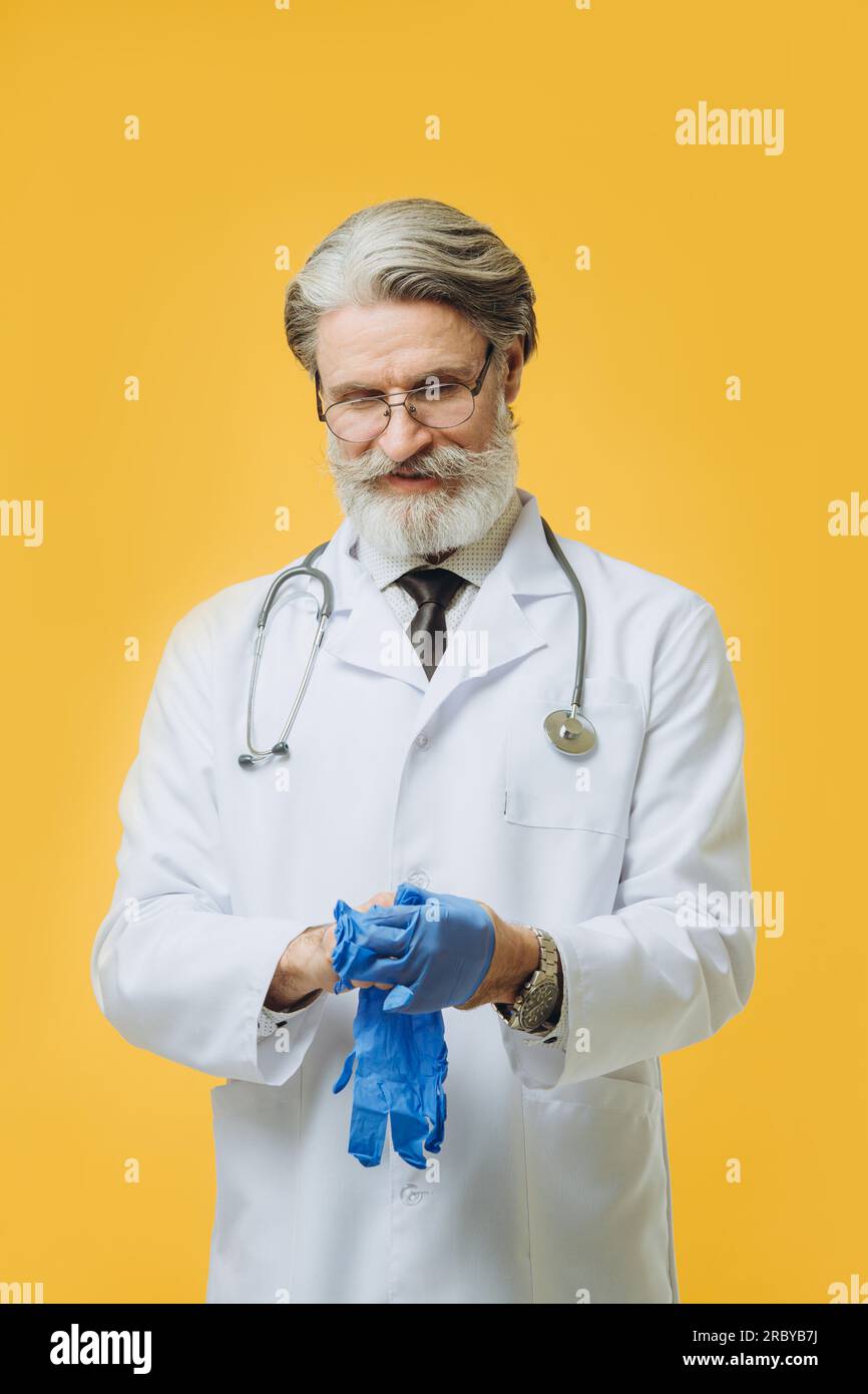 Mature doctor putting on rubber gloves on a yellow background Stock ...
