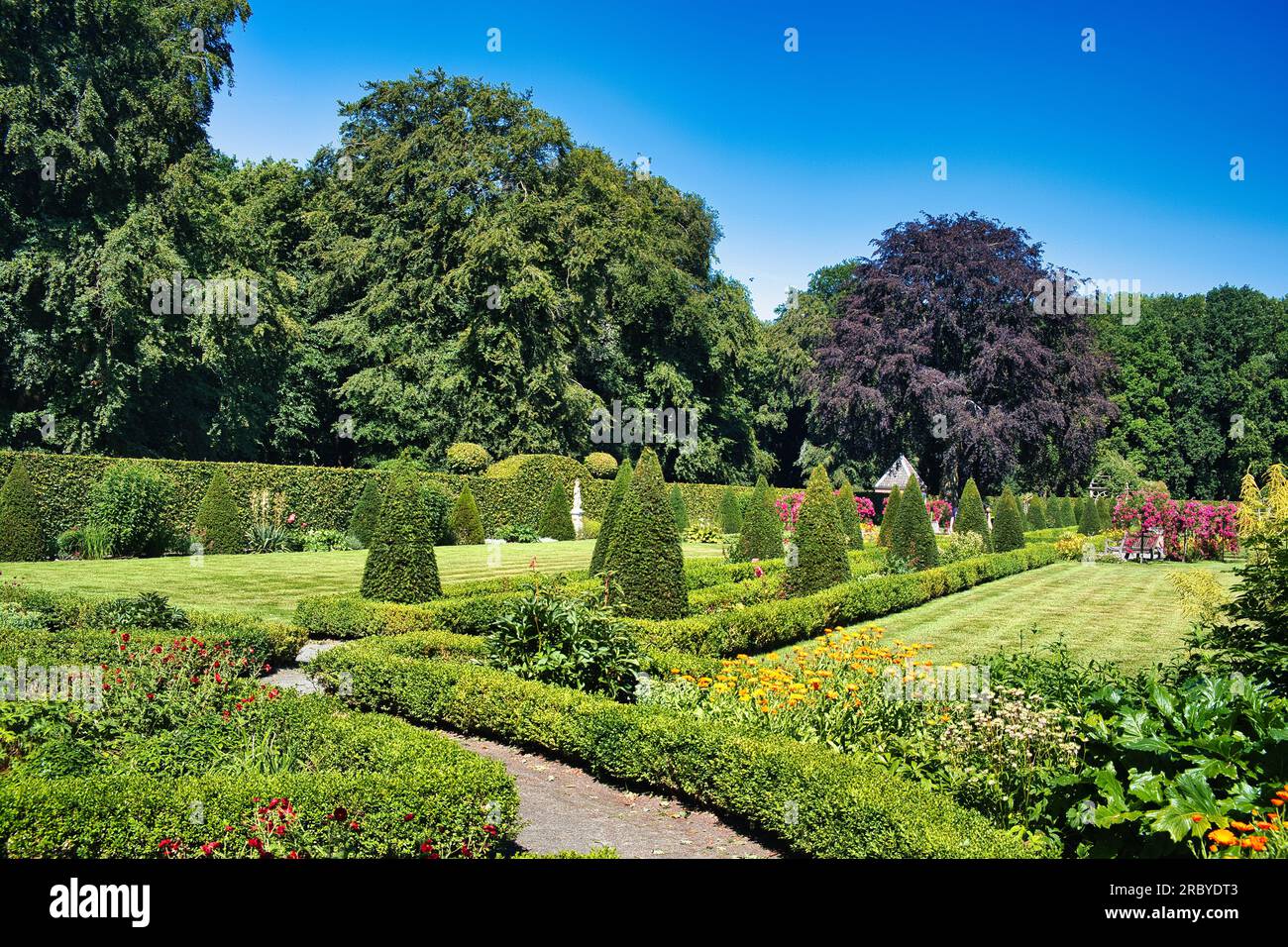 Formal French garden with topiary, flower beds, hedges, lawns and tall trees around castle ...
