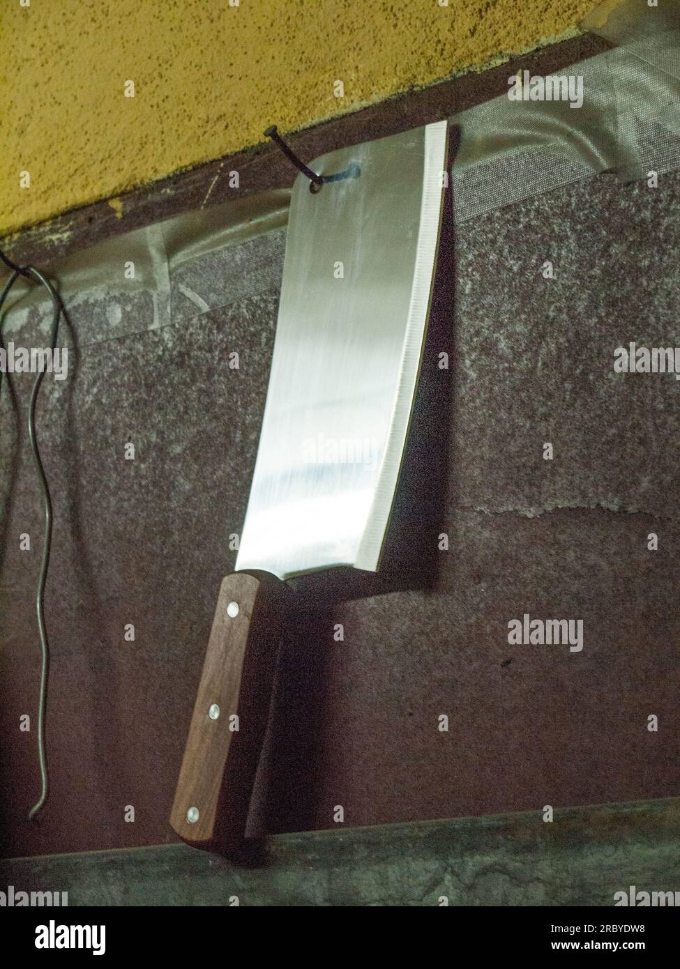 Meat cleaver with wooden handle hangs from a nail on a kitchen wall in ...