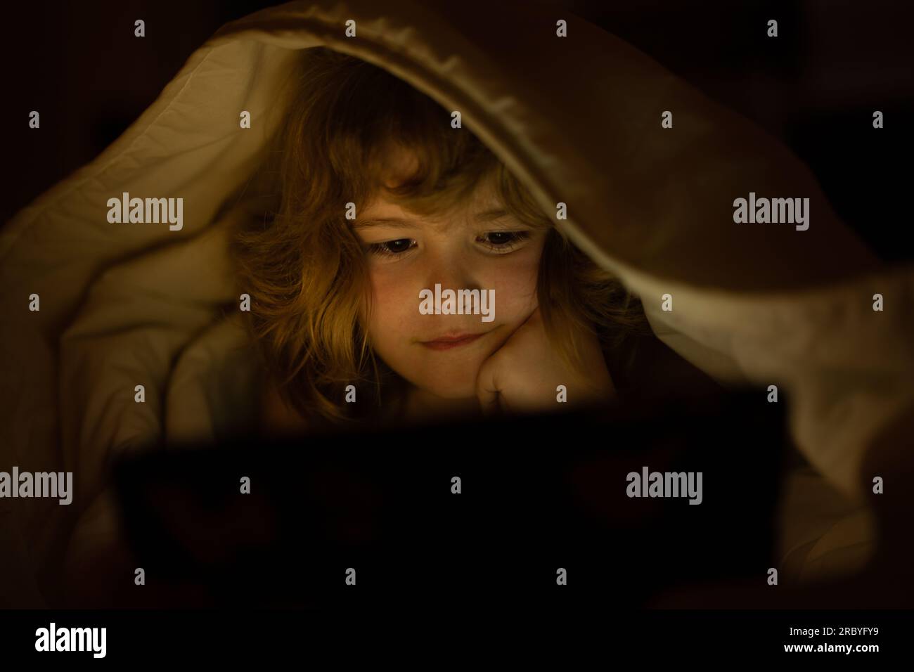Kid lying in bed at night and playing digital tablet. Child watching ...