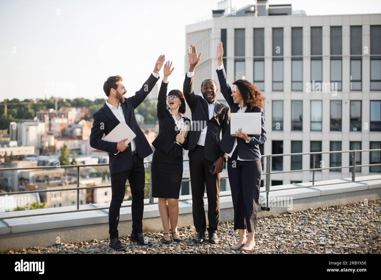 Group of diverse colleagues celebrating shared corporate success and raising hands in air ...