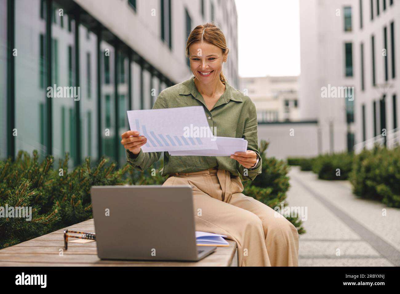 Woman analyst working with documents and use laptop sitting outside on ...
