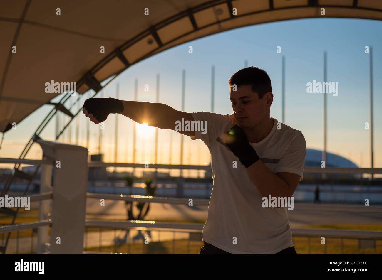 A man trains in boxing at the stadium at sunset. Athlete silhouette ...