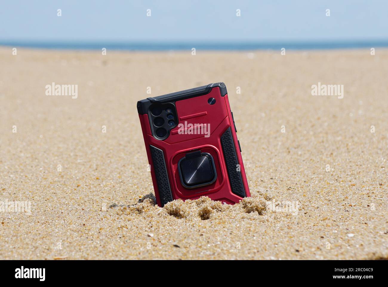 A red smartphone half-buried in the sand on the beach Stock Photo - Alamy