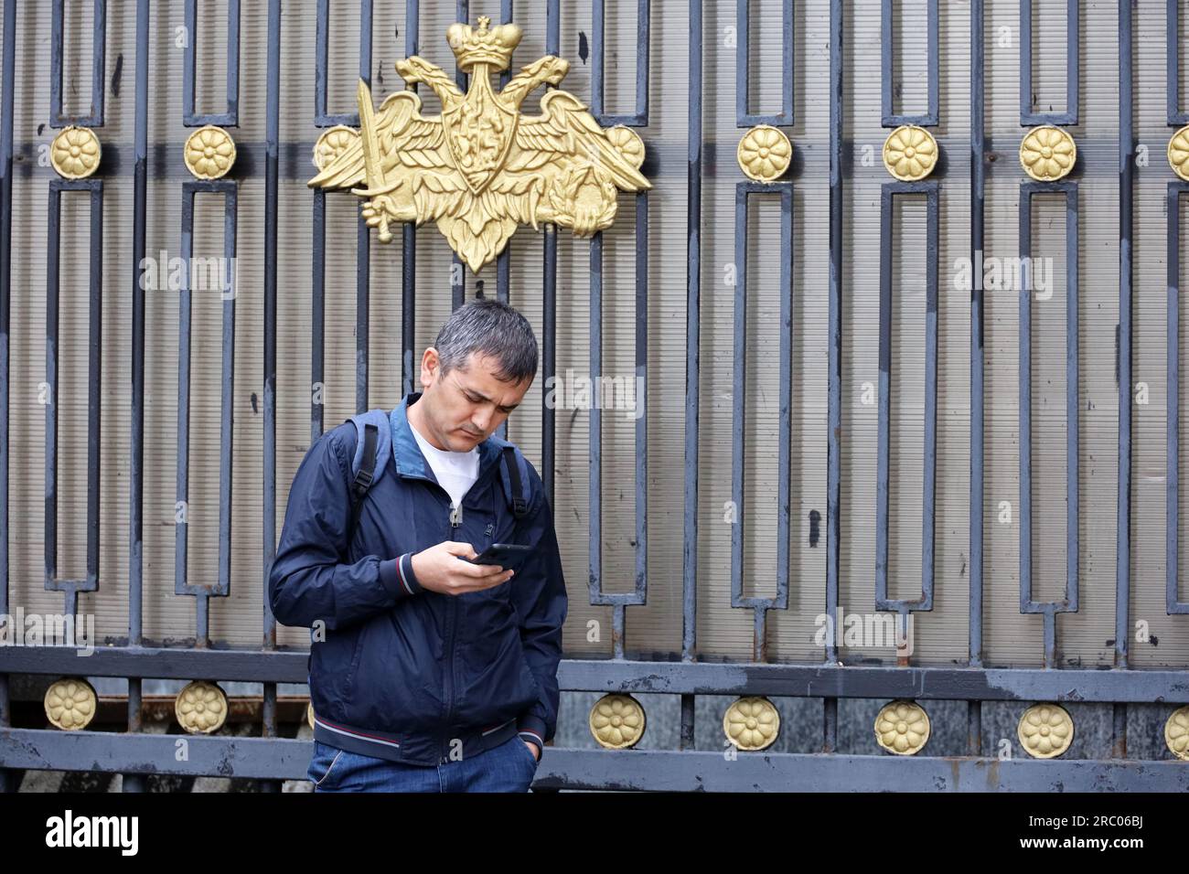 Man with mobile phone standing on city street near the fence with ...