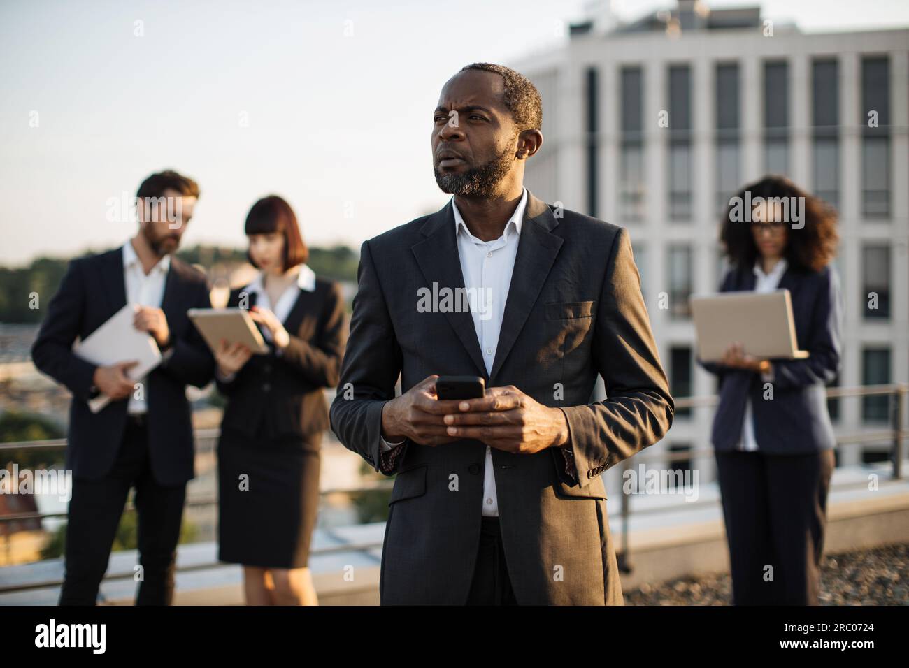 Good-looking corporate investor standing with smartphone in hands on ...