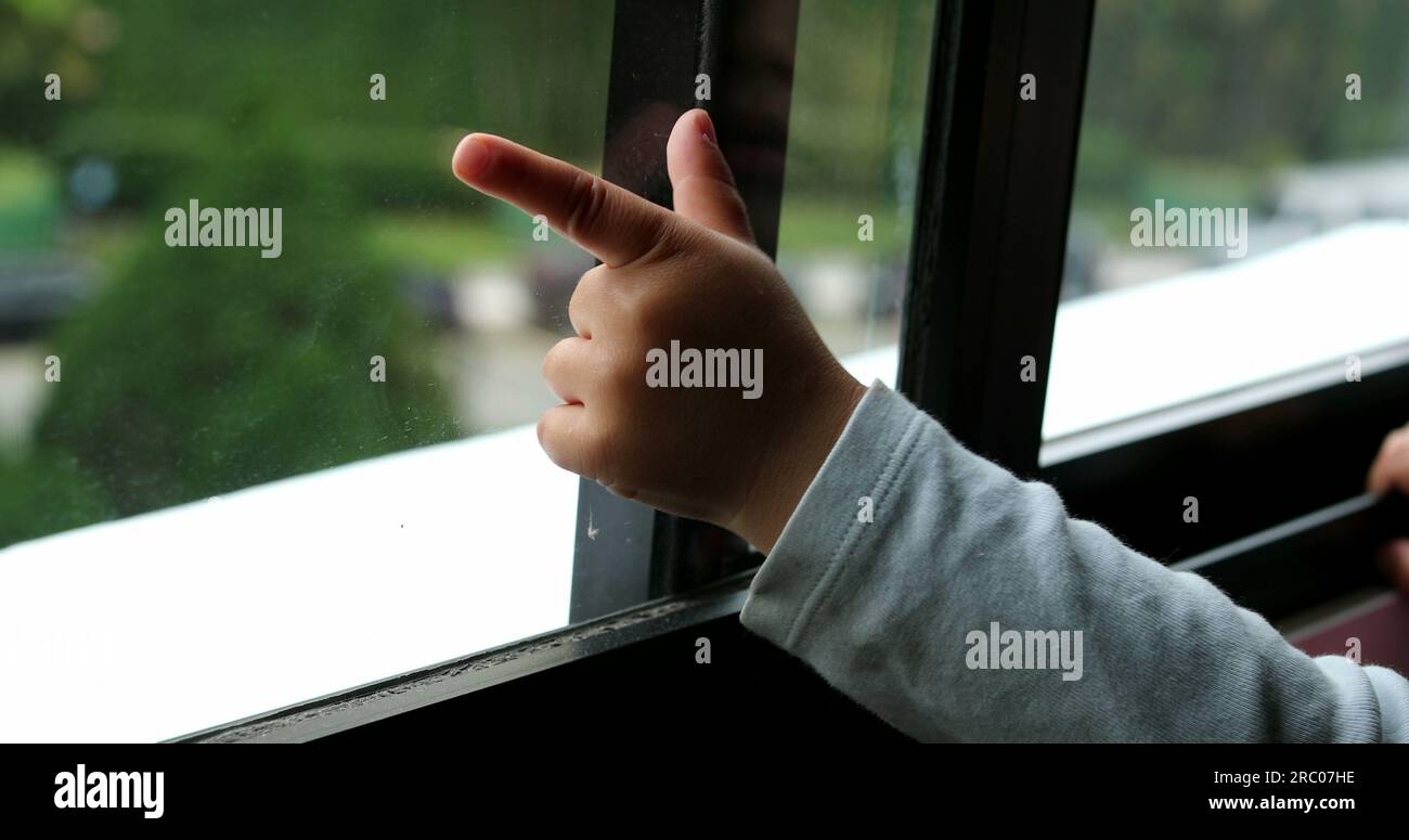 Little boy standing by window pointing outside with hand and finger ...