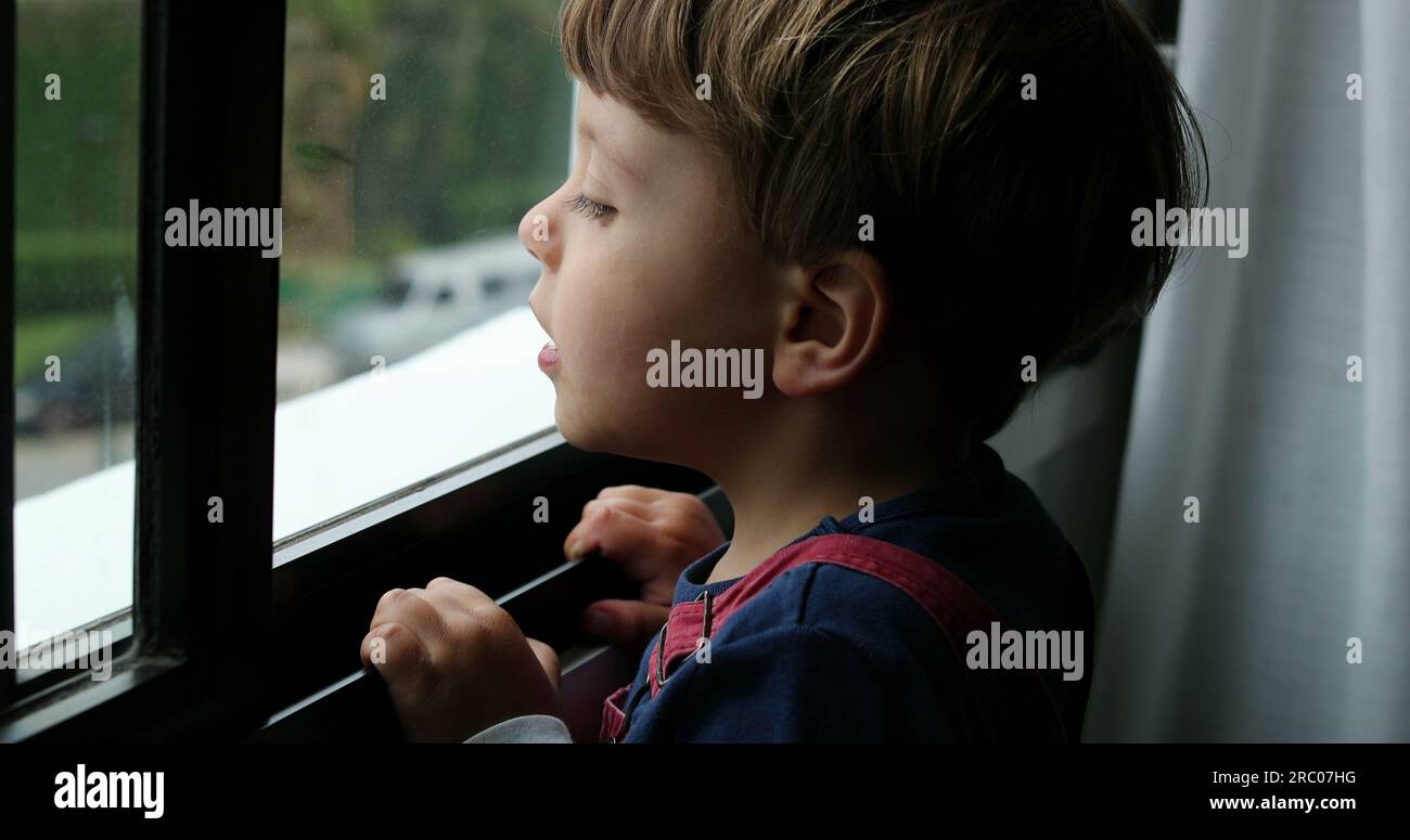 Kid standing by window looking outside child stares out leaning on ...