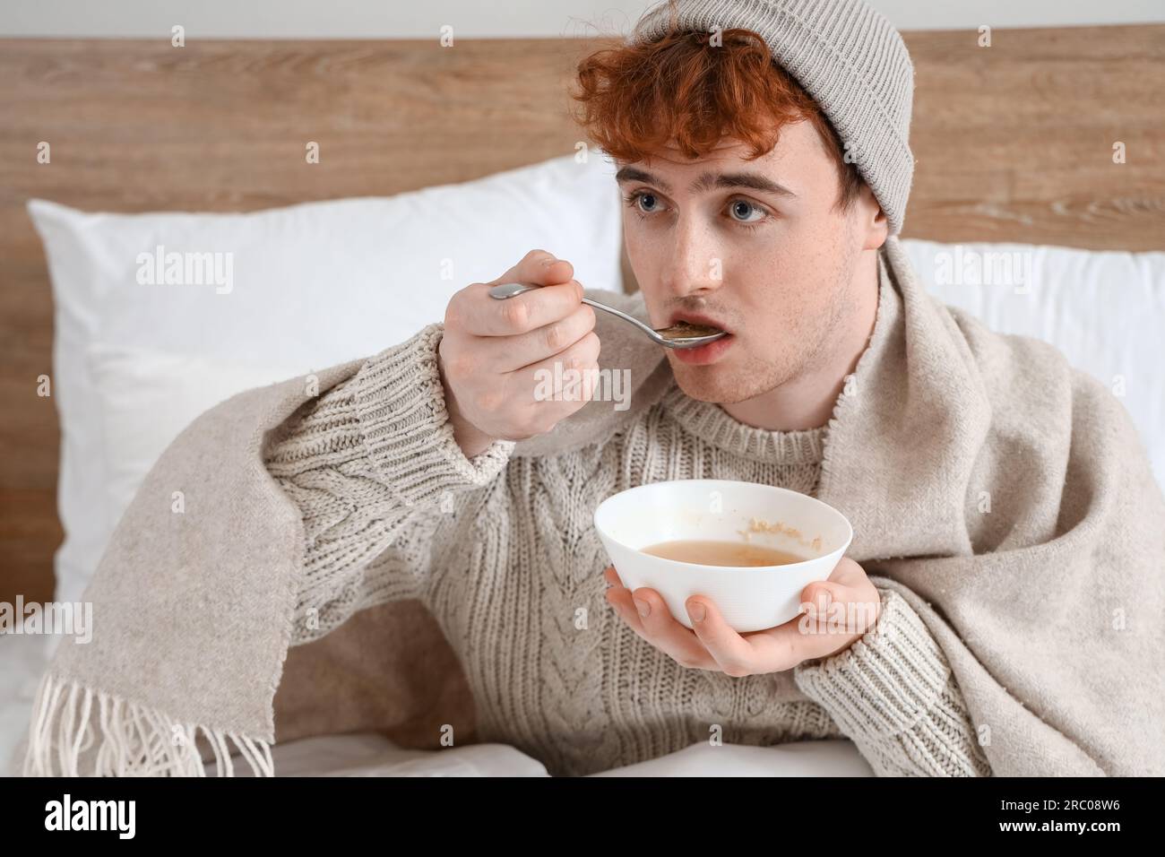 Ill young man eating soup in bedroom Stock Photo - Alamy