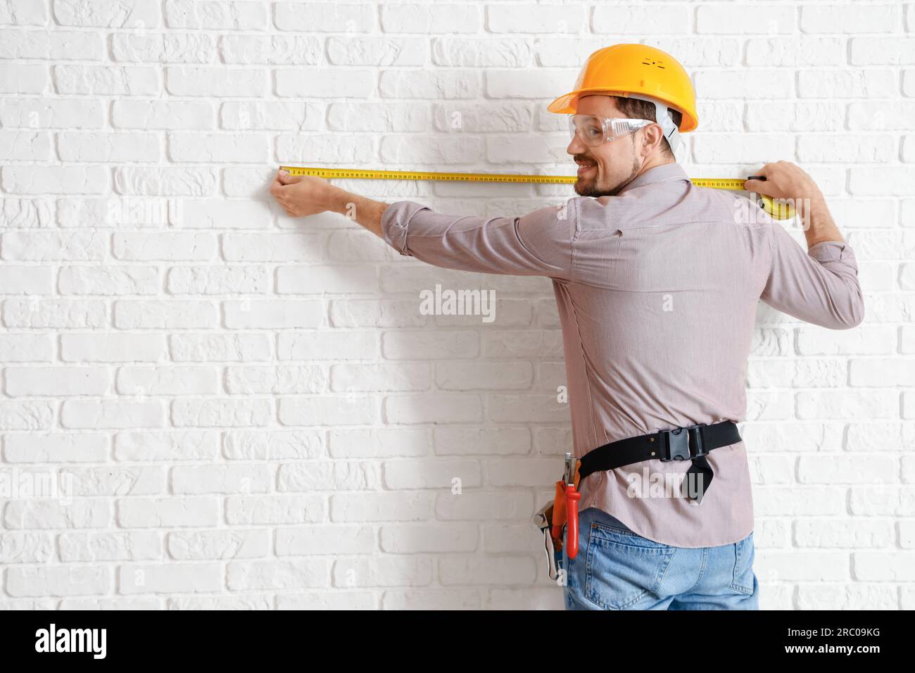 Male builder measuring white brick wall Stock Photo - Alamy