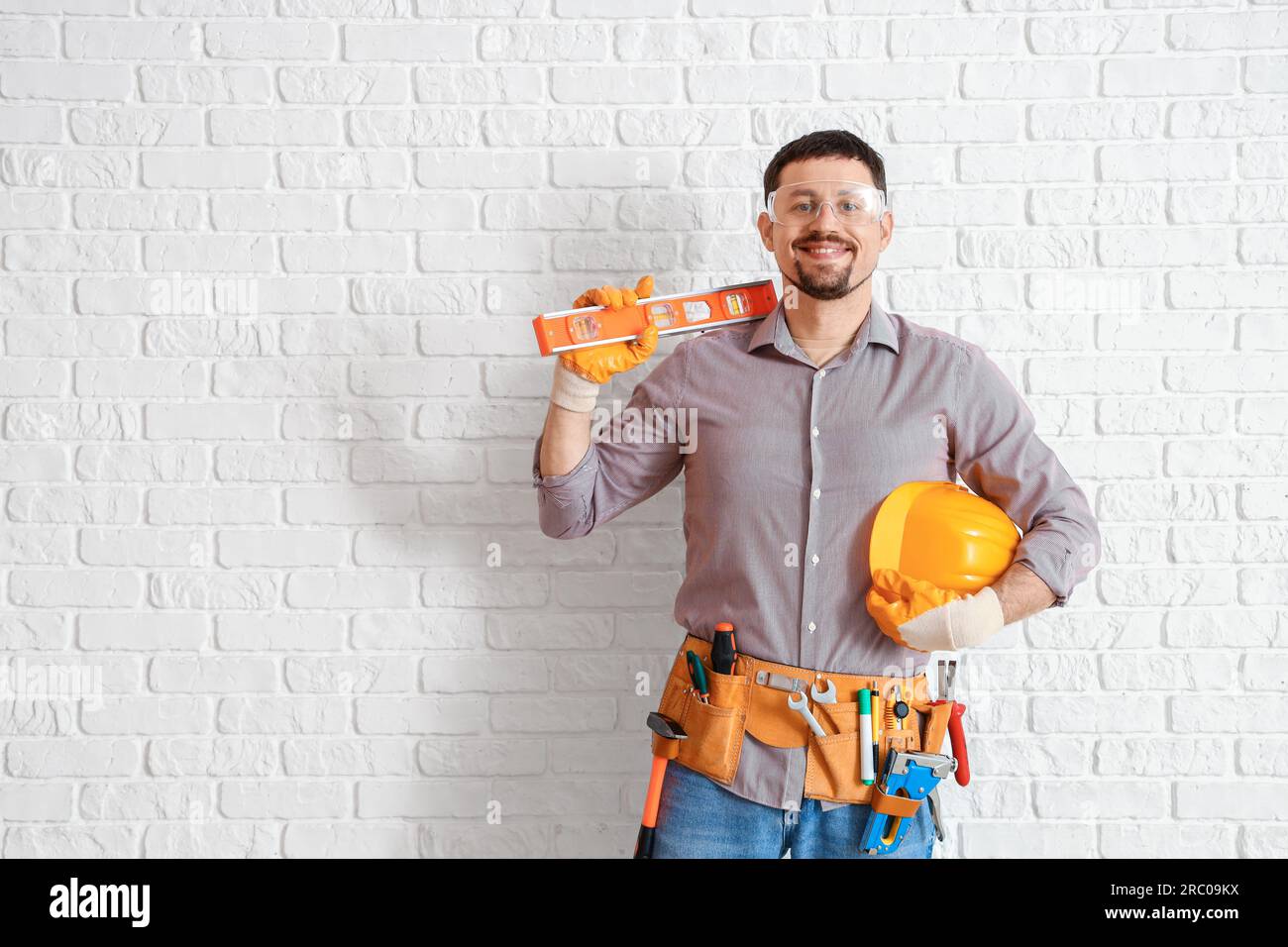 Male builder with tools near white brick wall Stock Photo - Alamy