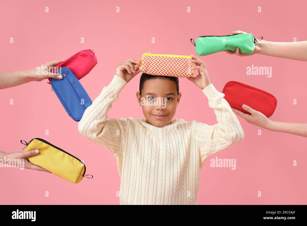 Little African-American boy and female hands with pencil cases on pink ...