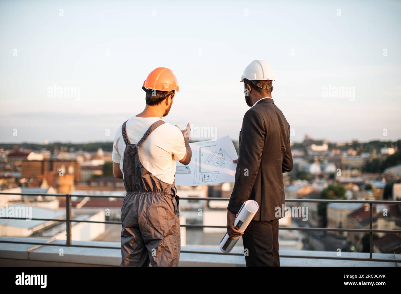 Back view of two male builders in protective helmets watching at ...