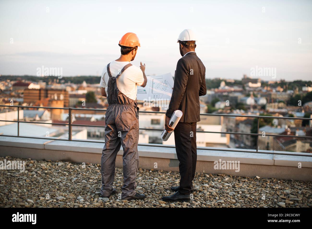 Back view of two male builders in protective helmets watching at ...
