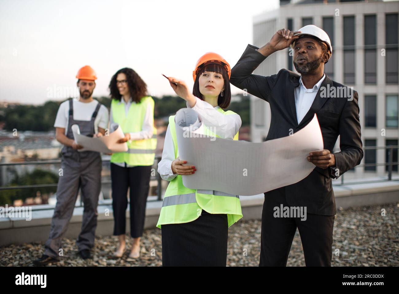 Group of diverse engineers with blueprints standing on flat rooftop and ...