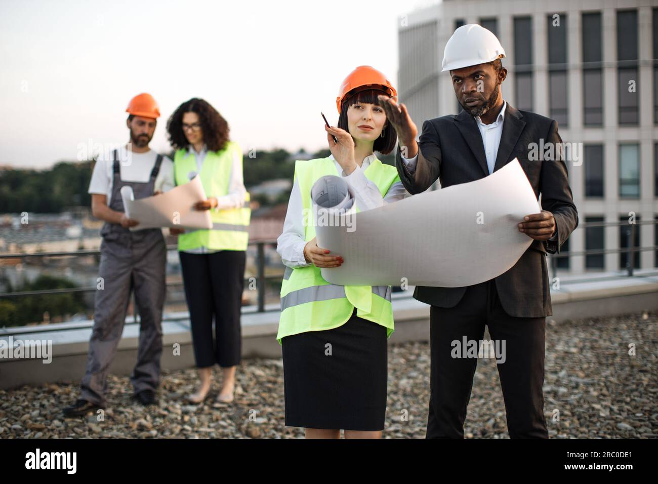 Group of diverse engineers with blueprints standing on flat rooftop and ...