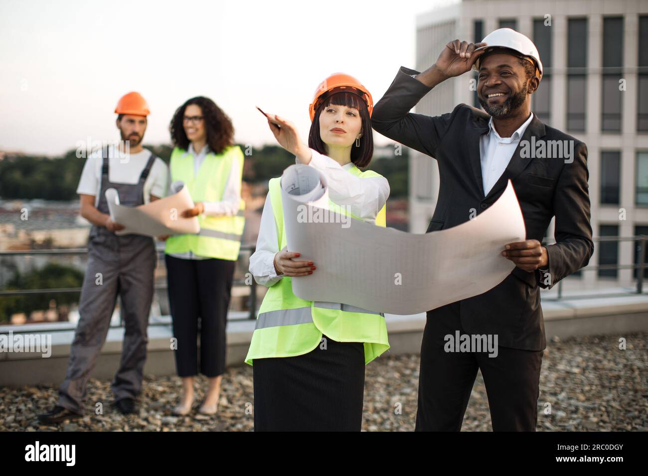Group of diverse engineers with blueprints standing on flat rooftop and ...
