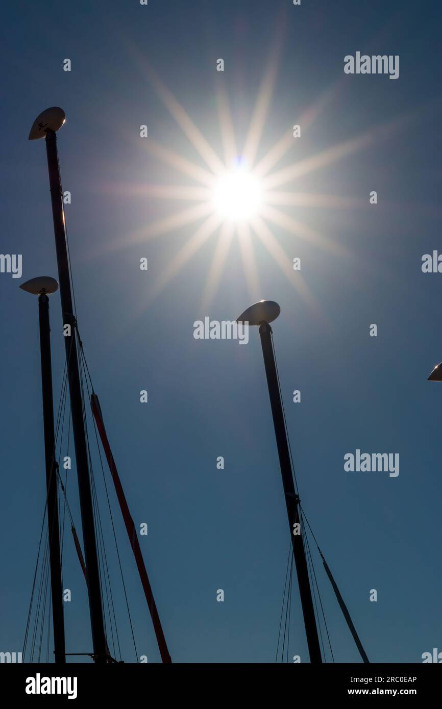 Low angle view of masts of sailing boats against sun in the shape of a ...