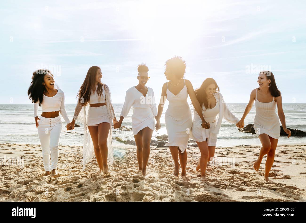 Full length shot of happy ladies walking on the sea shore, holding ...
