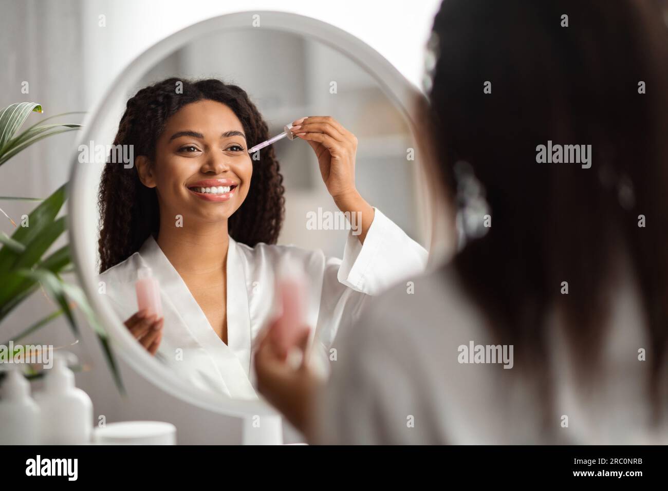 Eye Zone Care. Happy beautiful black woman applying eyes serum near ...