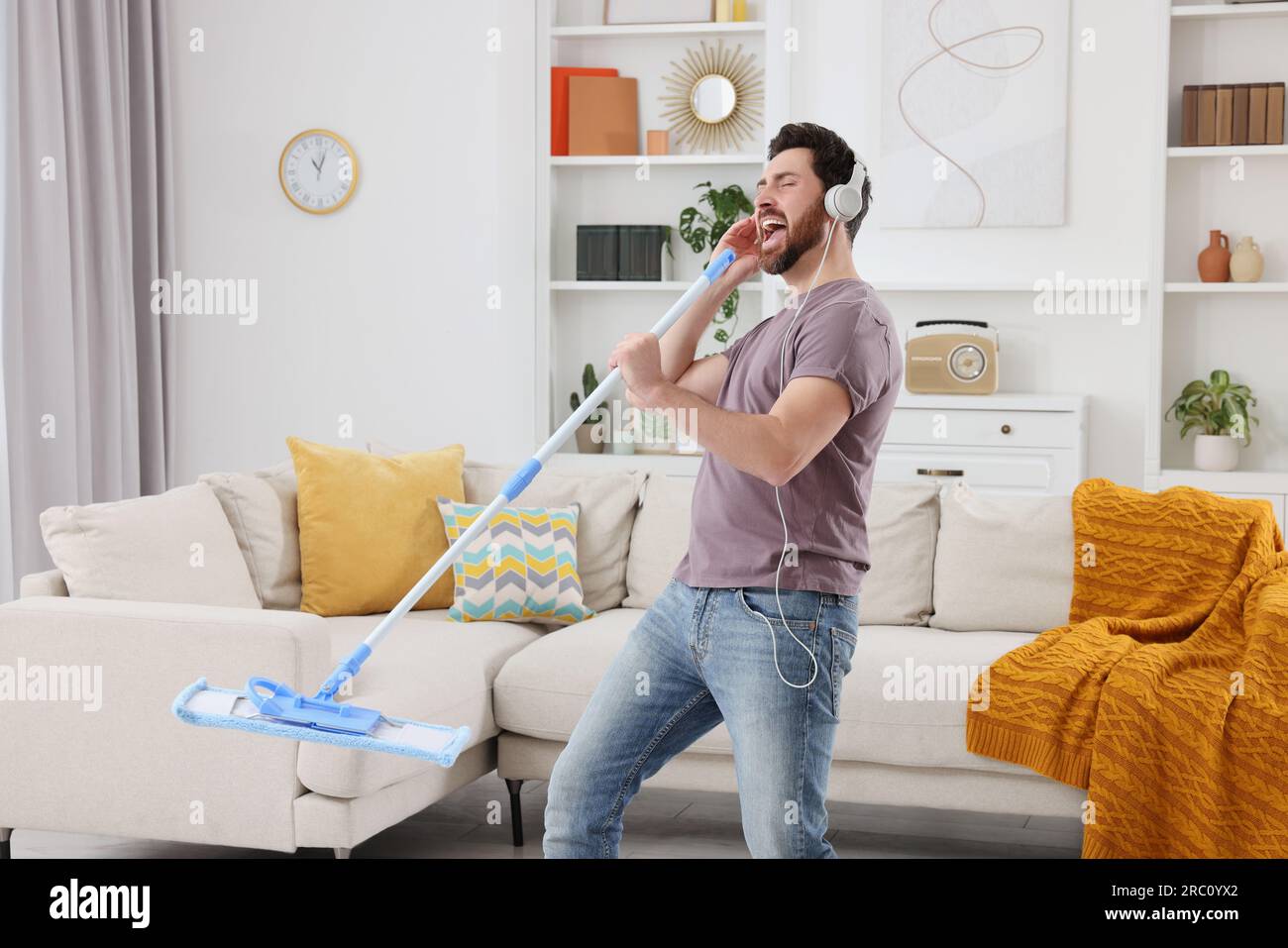 Spring cleaning. Man in headphones with mop singing while tidying up ...