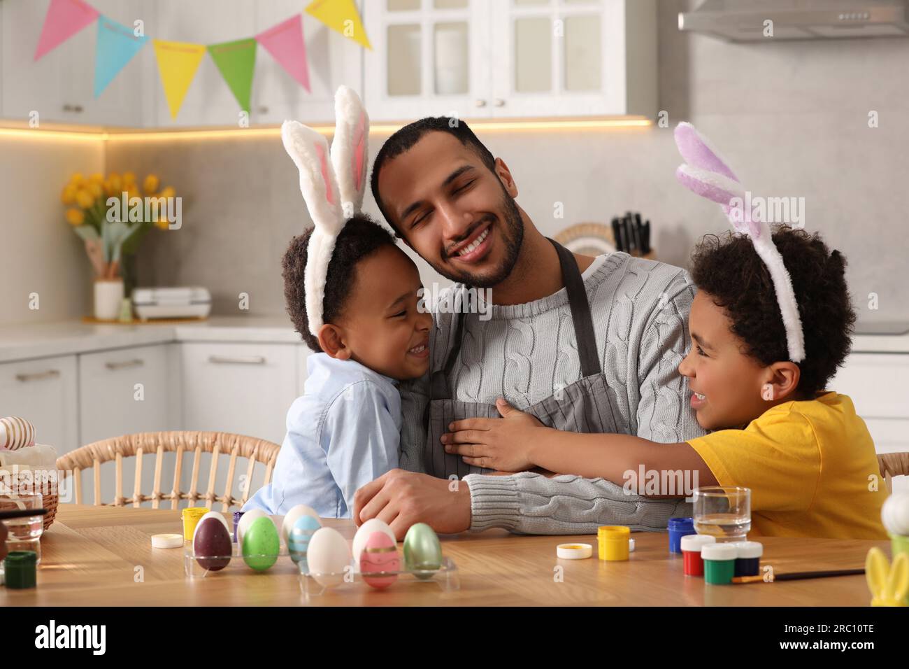 Happy African American father hugging his cute children and Easter eggs ...