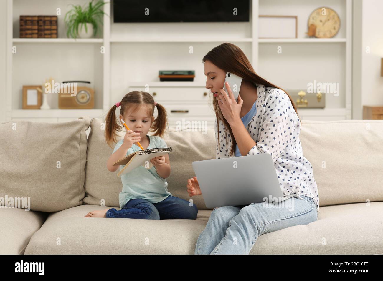 Working remotely at home. Mother watching over her daughter on sofa in ...