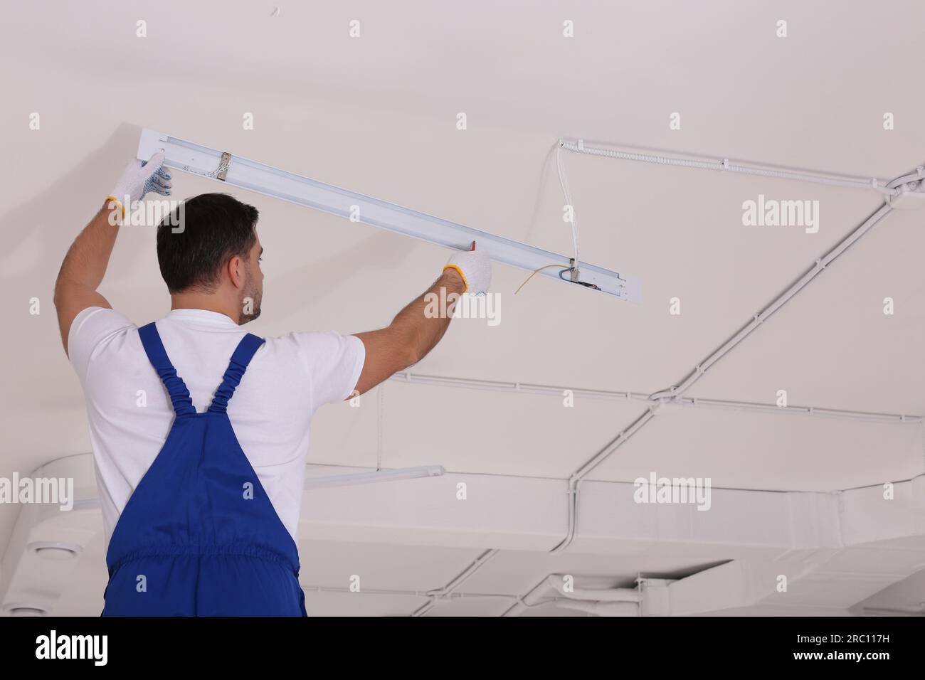 Ceiling light. Electrician installing led linear lamp indoors, back ...