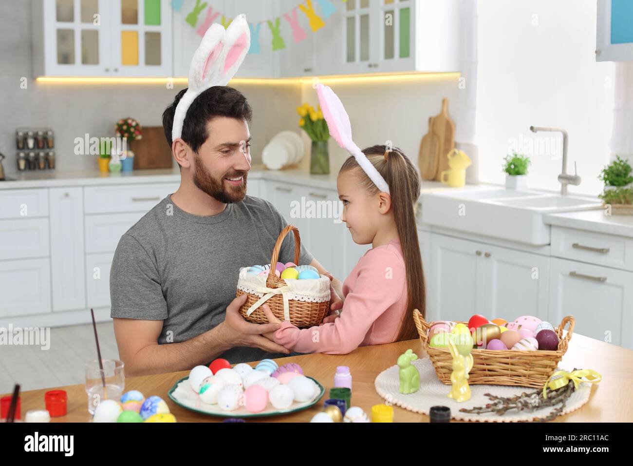 Father and his cute daughter with wicker basket full of Easter eggs in ...