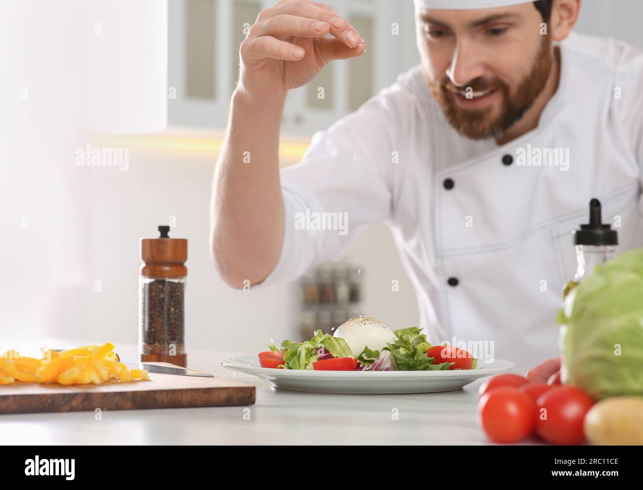 Professional chef salting delicious salad at marble table, focus on ...