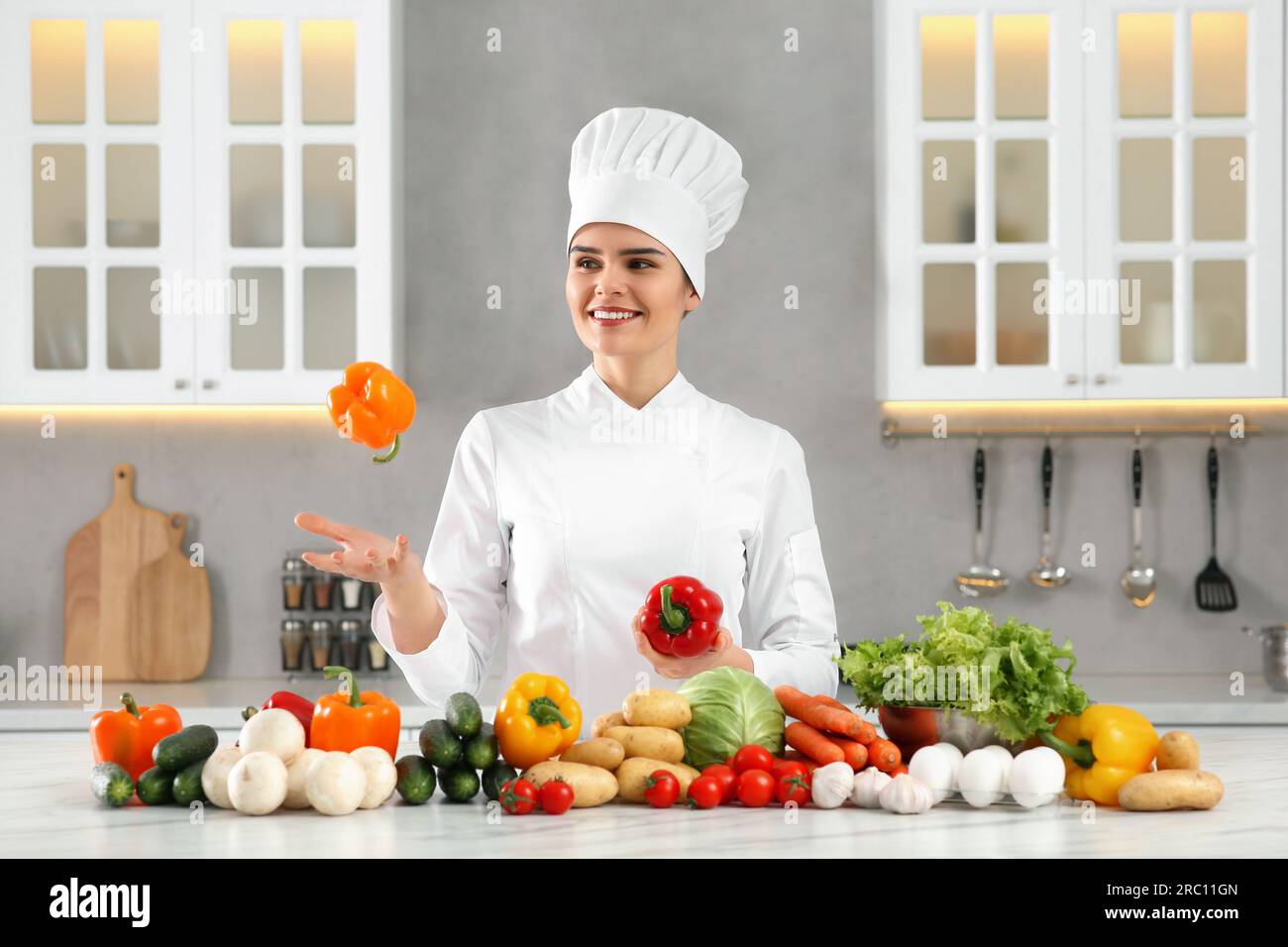 Happy chef throwing bell pepper near fresh vegetables at table in ...