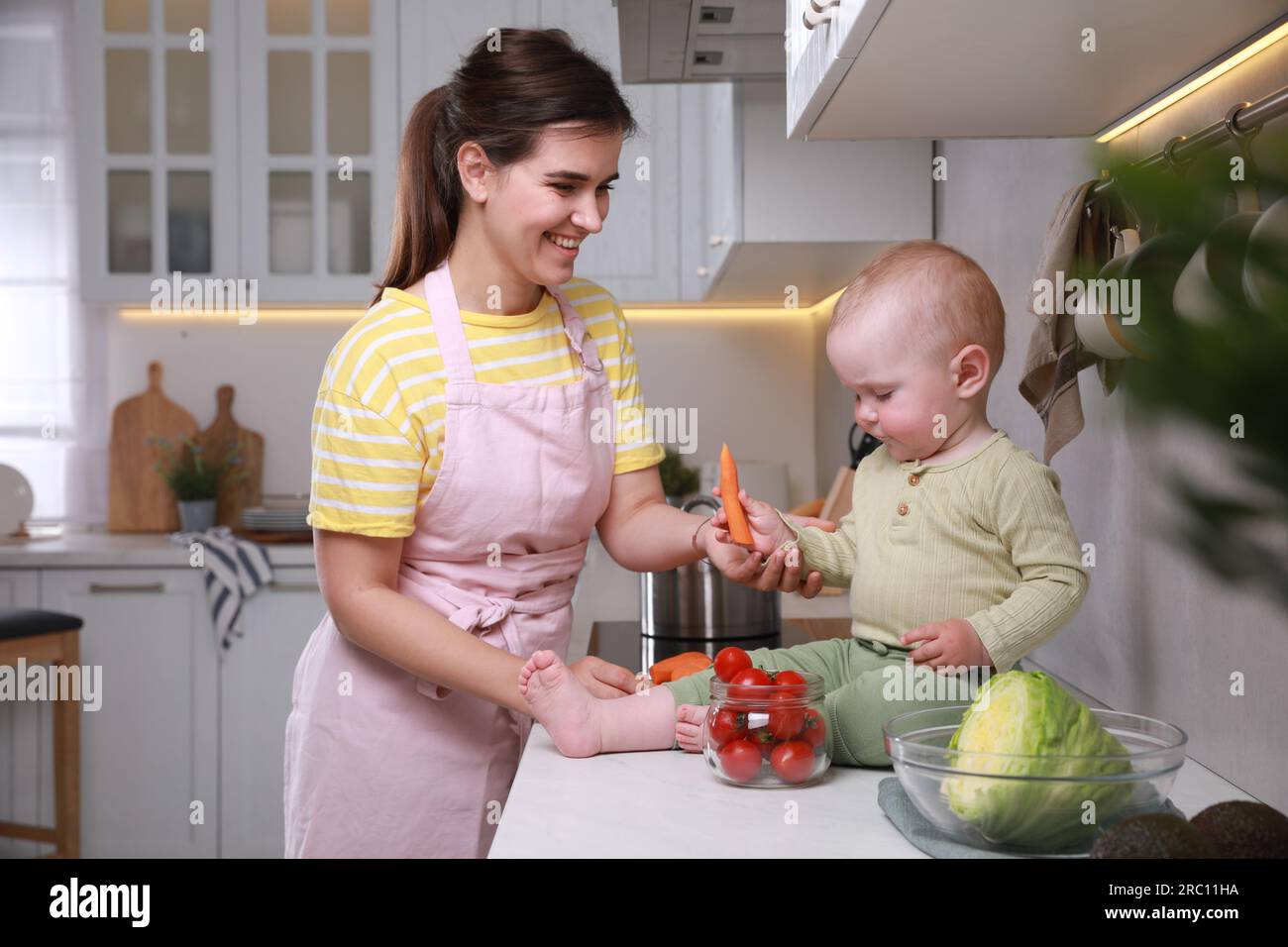 Happy young woman and her cute little baby cooking together in kitchen ...