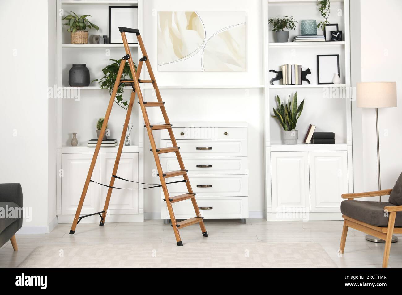 Wooden folding ladder near chest of drawers and shelves with ...