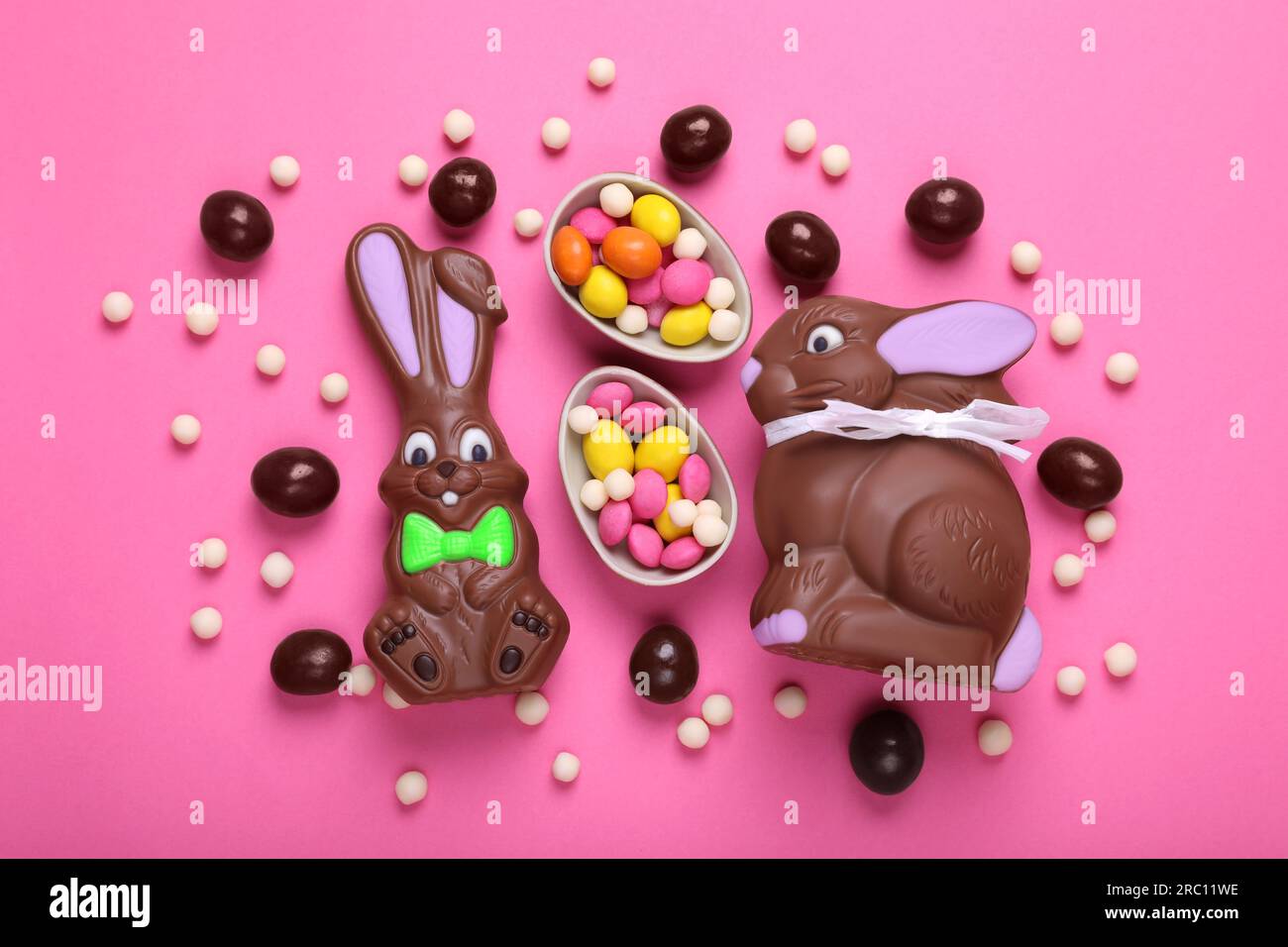 Chocolate Easter bunnies, halves of egg and candies on pink background ...