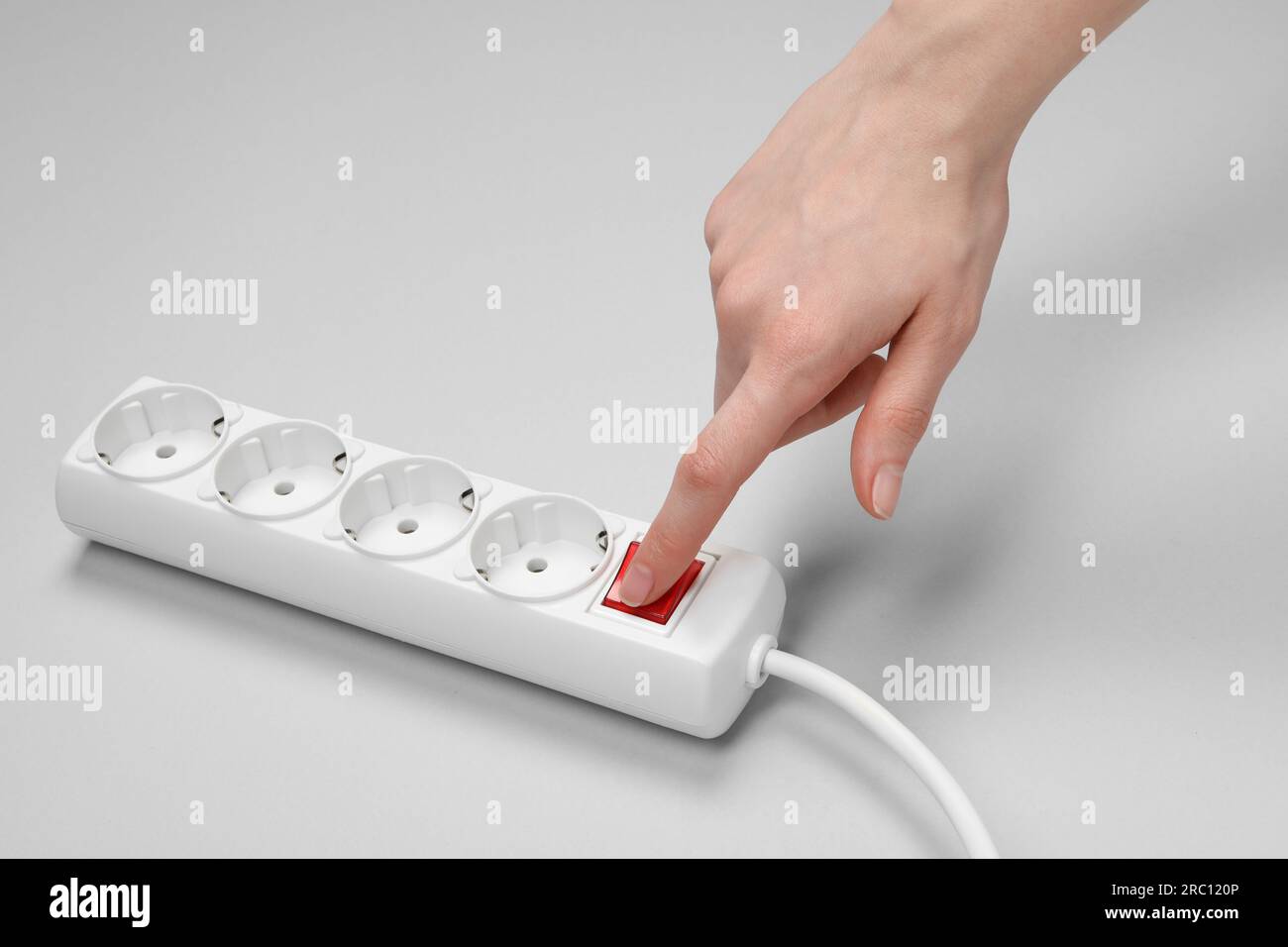 Woman pressing switch button of power strip on white background ...