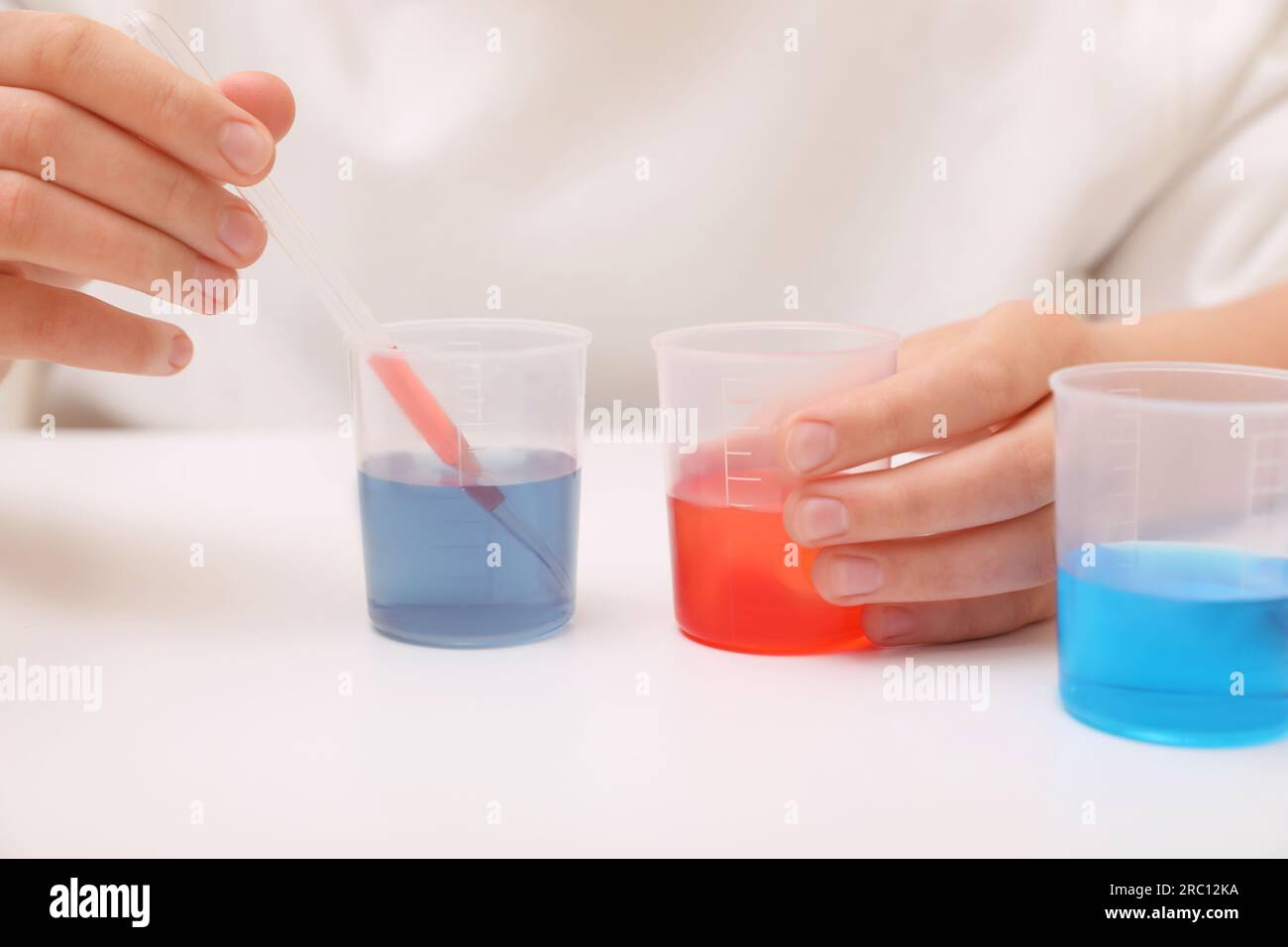 Girl mixing colorful liquids at white table indoors, closeup. Chemical ...