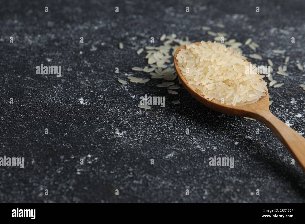 Spoon with raw rice on black textured table. Space for text Stock Photo ...