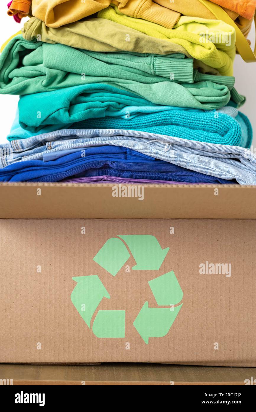 A stack of clothes in different colors in a box with a recycle sign ...