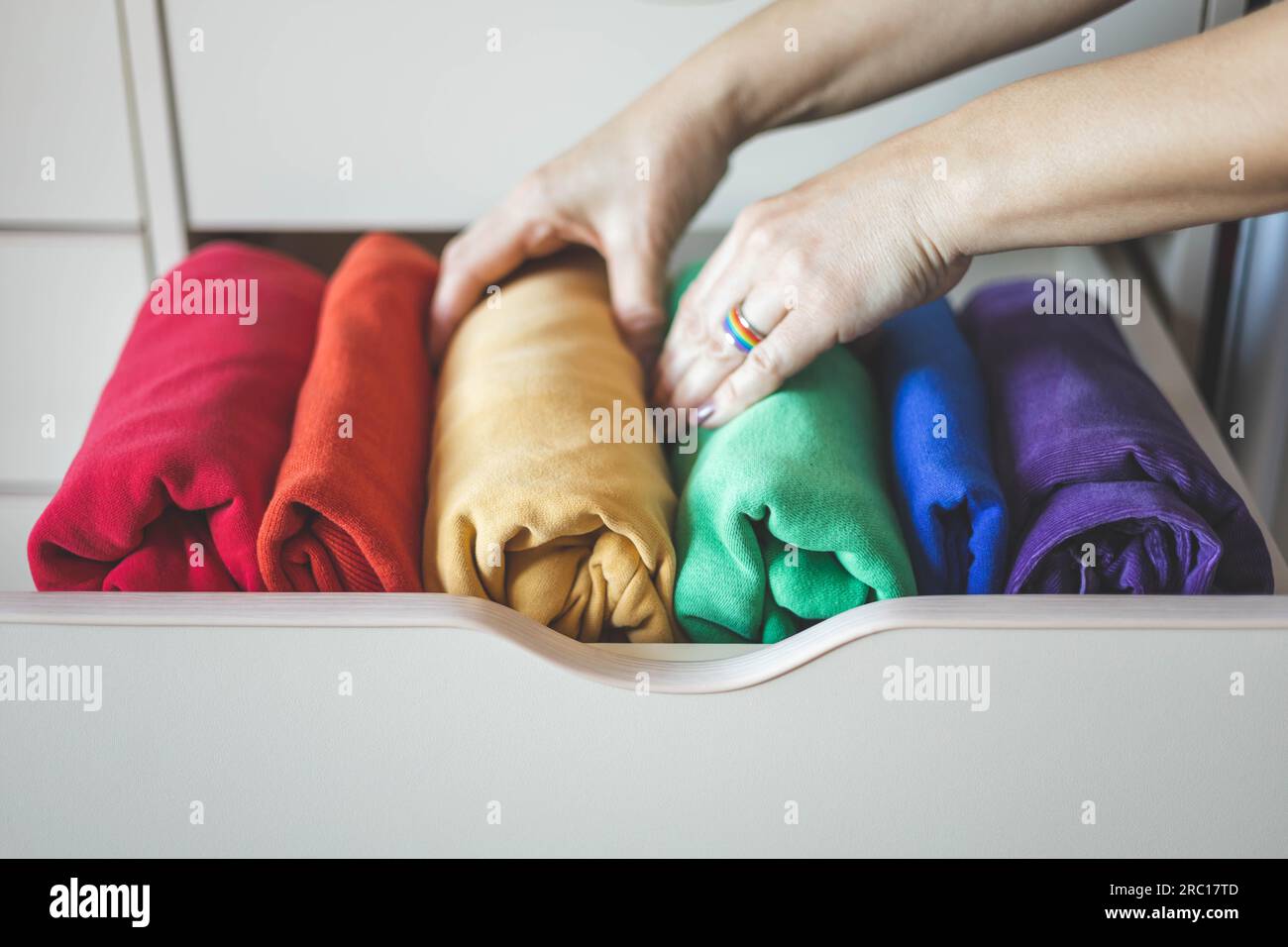 The colorful clothes are laid out in the colors of the LGBT flag. Hands ...