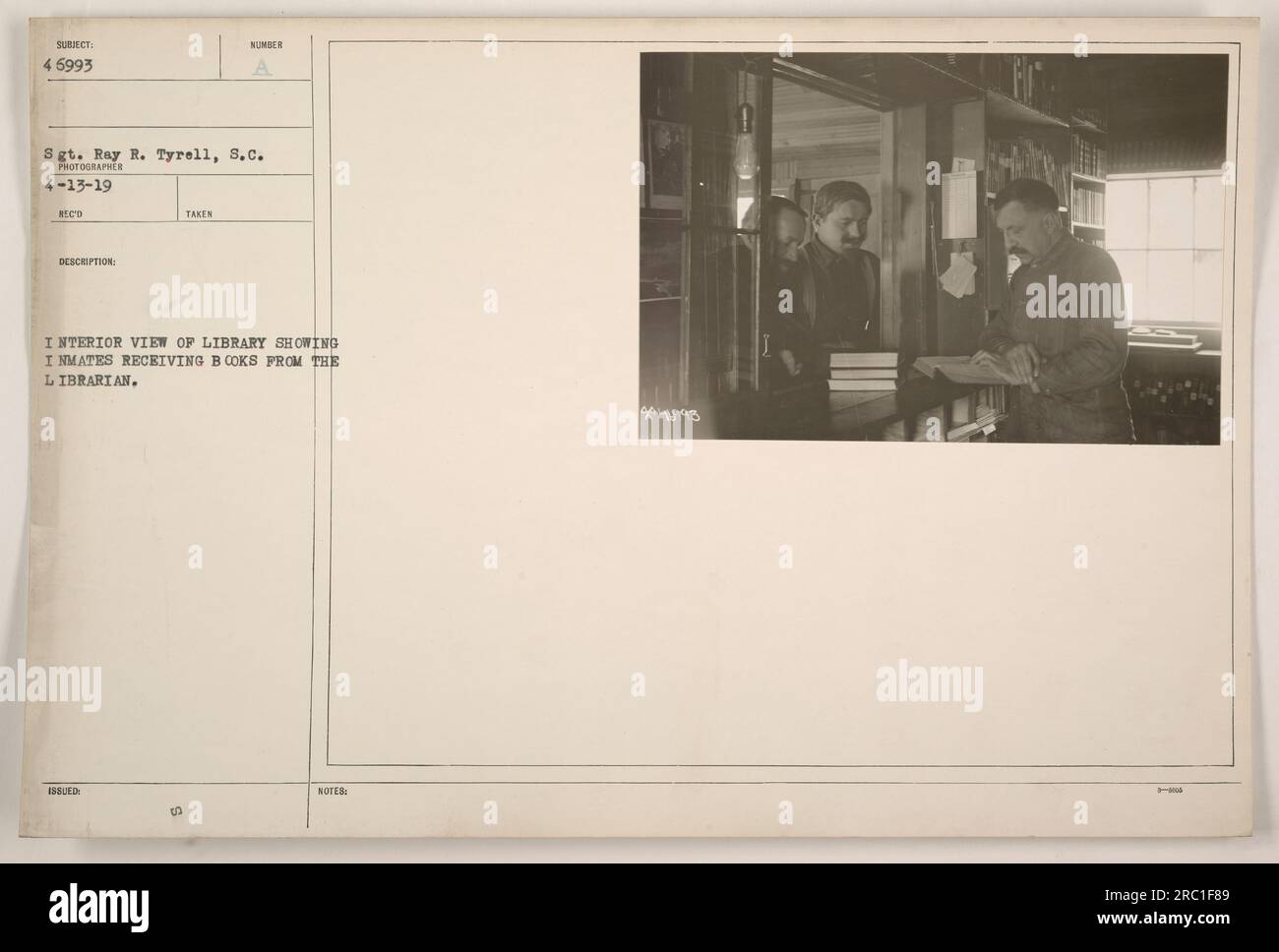 Inmates in a library receive books from the librarian. Photograph ...