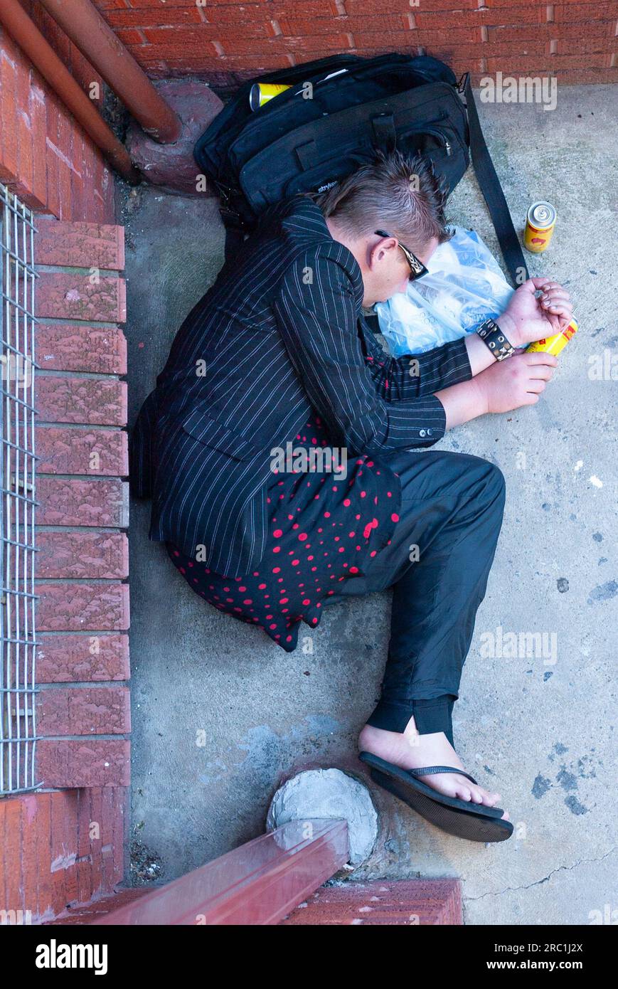 A homeless young man passed out on a sidewalk, surrounded by empty cans ...