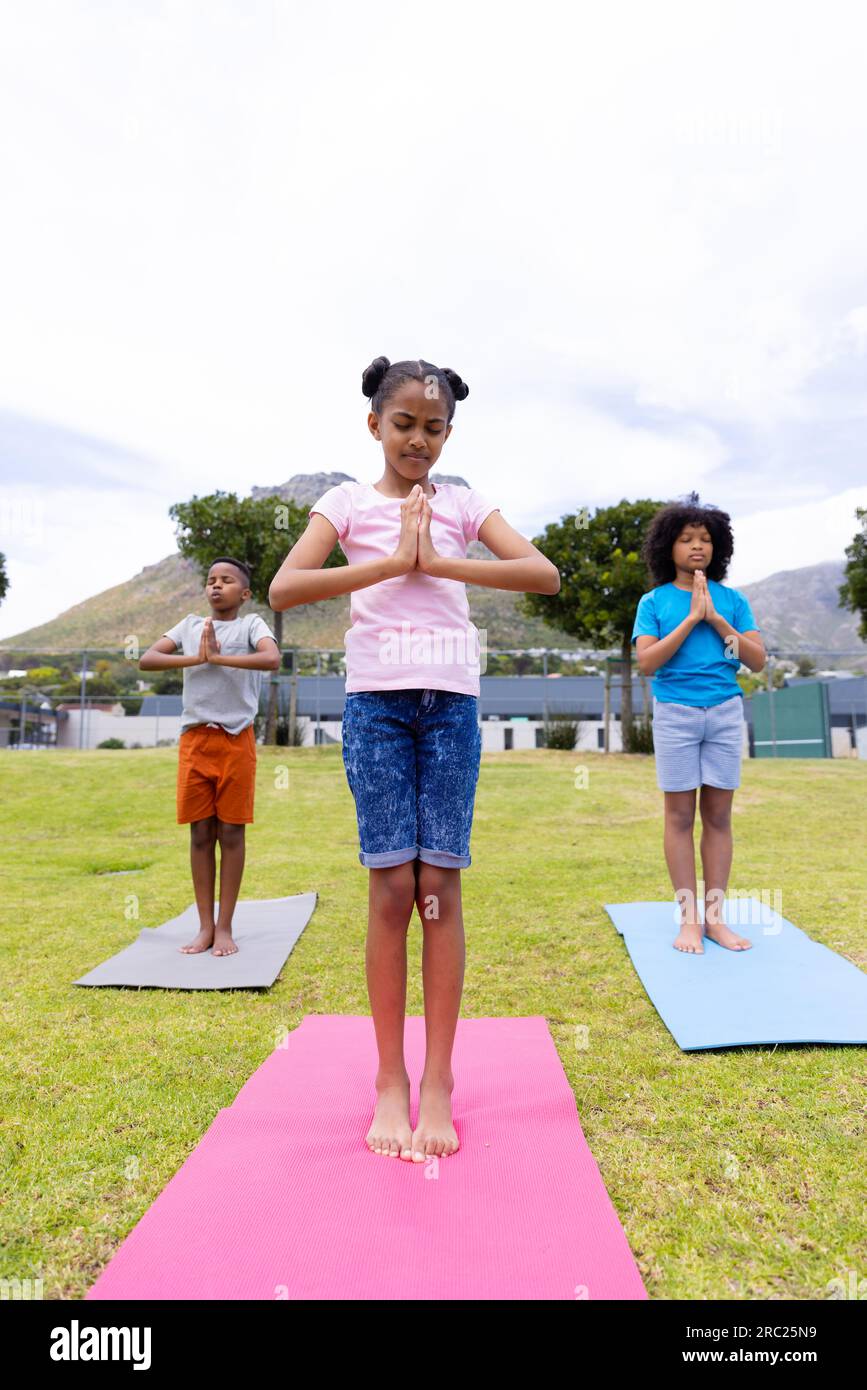 Happy african american schoolchildren doing yoga and meditating on ...