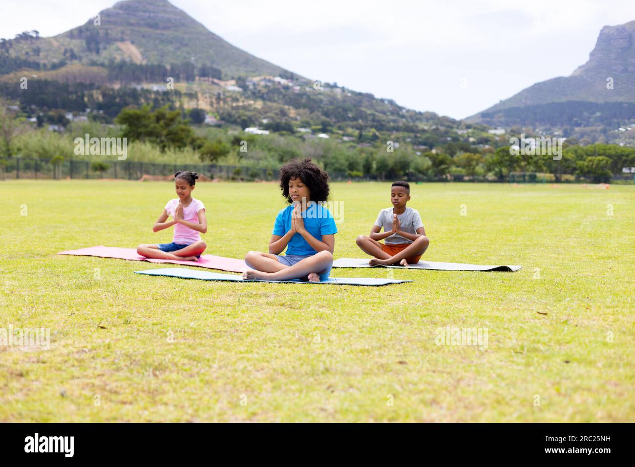 Happy african american schoolchildren doing yoga and meditating on ...