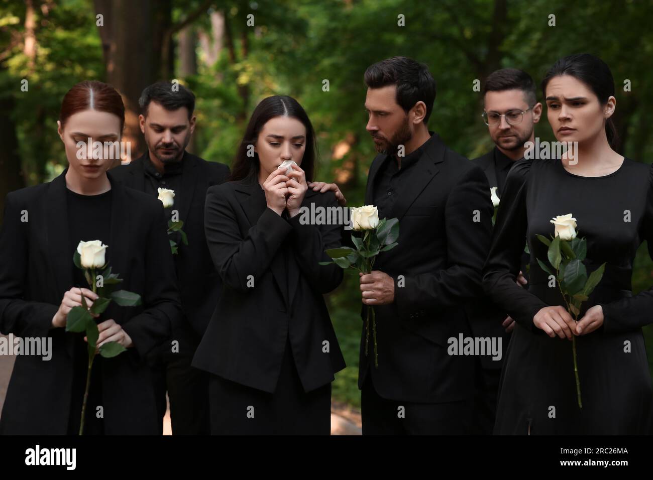 Funeral ceremony. Sad people with white rose flowers mourning outdoors ...