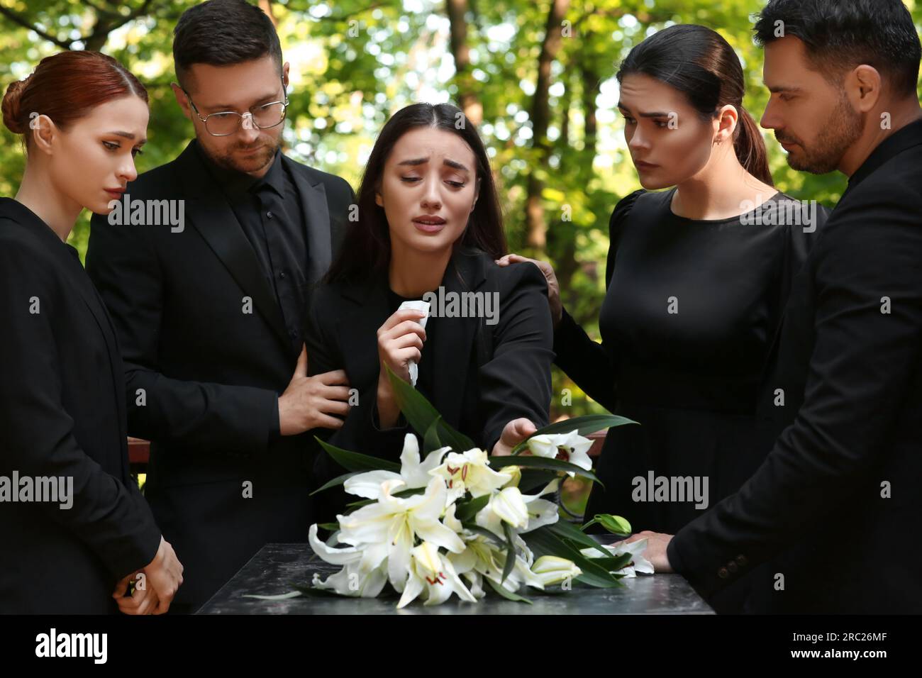 Funeral ceremony. Sad people mourning near granite tombstone with white ...