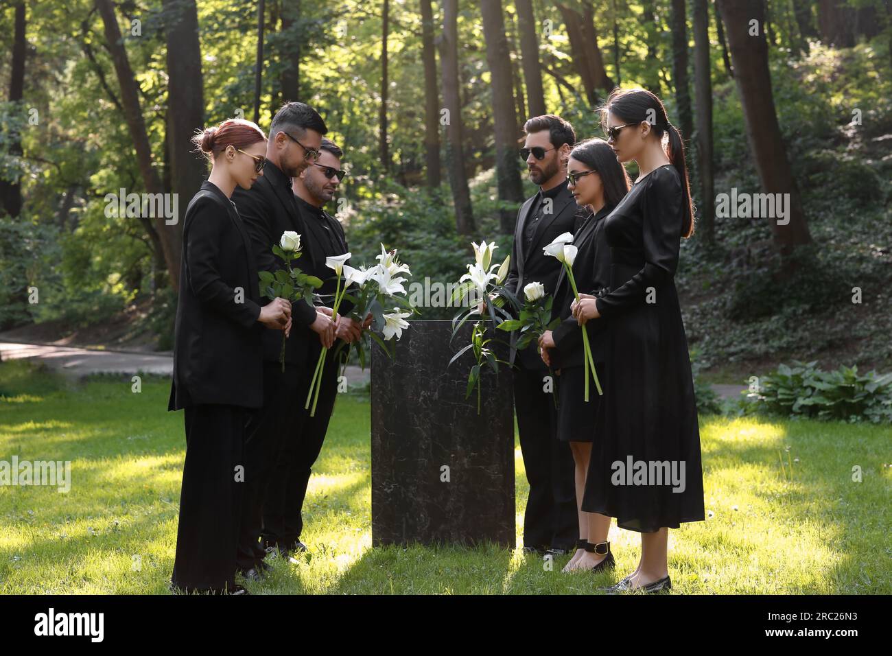 Sad people with flowers mourning near granite tombstone at cemetery ...